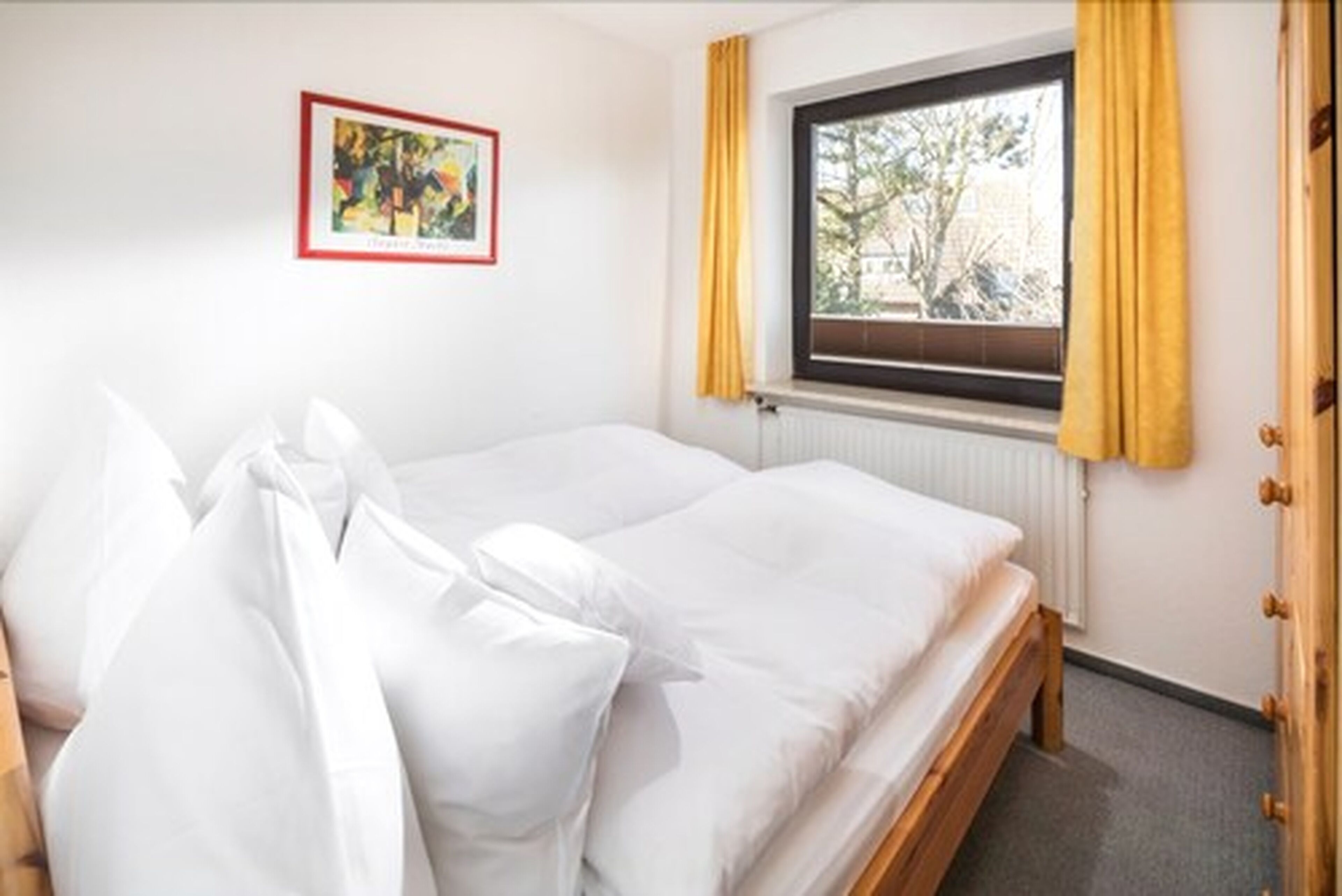 Quarto individual com uma janela, um radiador e um quadro emoldurado na parede.