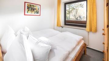 Quarto individual com uma janela, um radiador e um quadro emoldurado na parede.