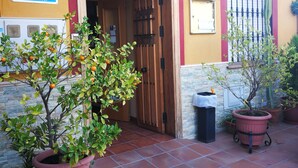 Entrada de hotel com porta de madeira, plantas em vasos e uma placa com a inscrição 'CASA AZQUEZ'.