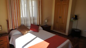 Quarto com cama, travesseiros, mesa de cabeceira, abajur, guarda-roupa e uma pequena estante com objetos.