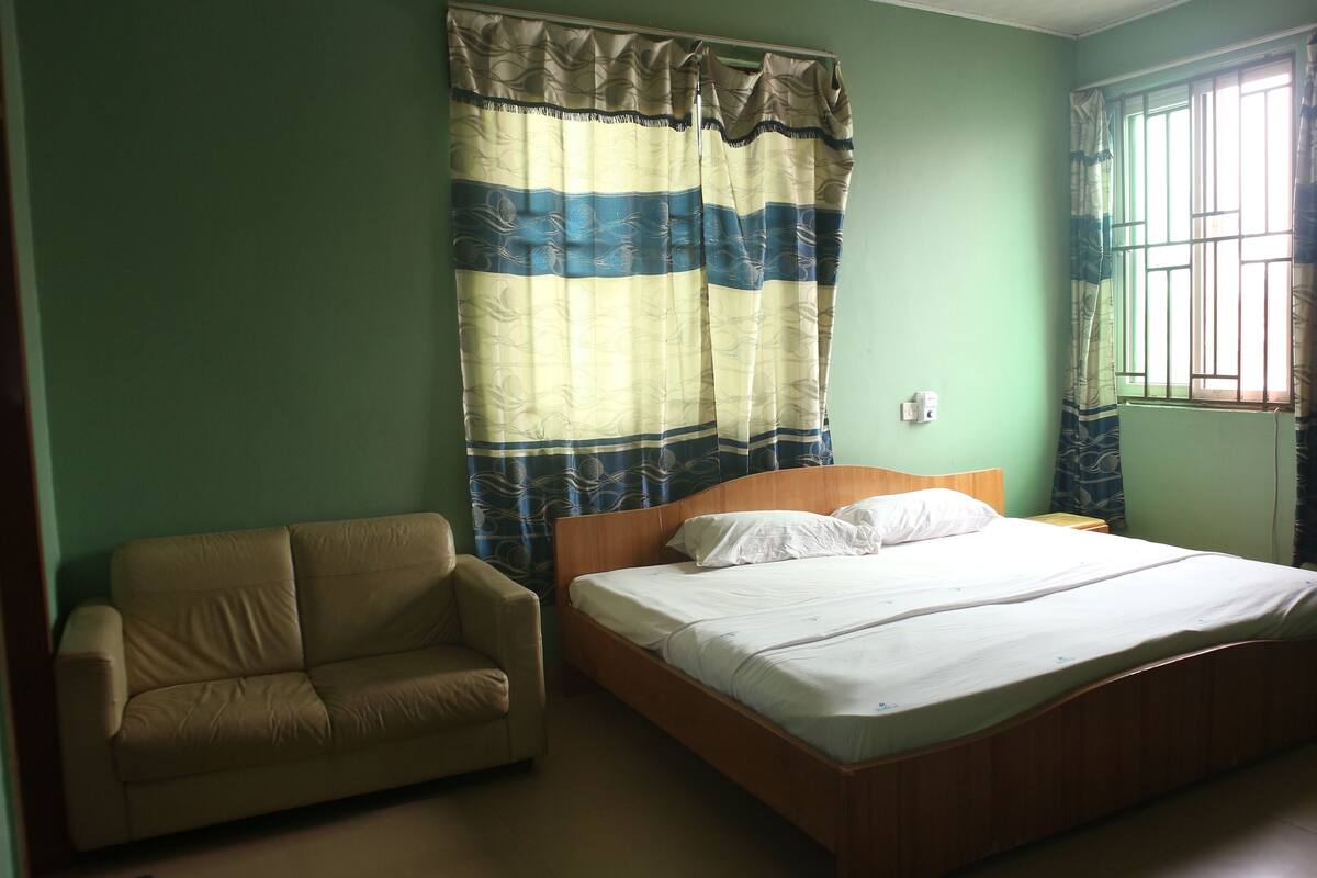 Quarto com cama, cadeira e janela com cortinas.
