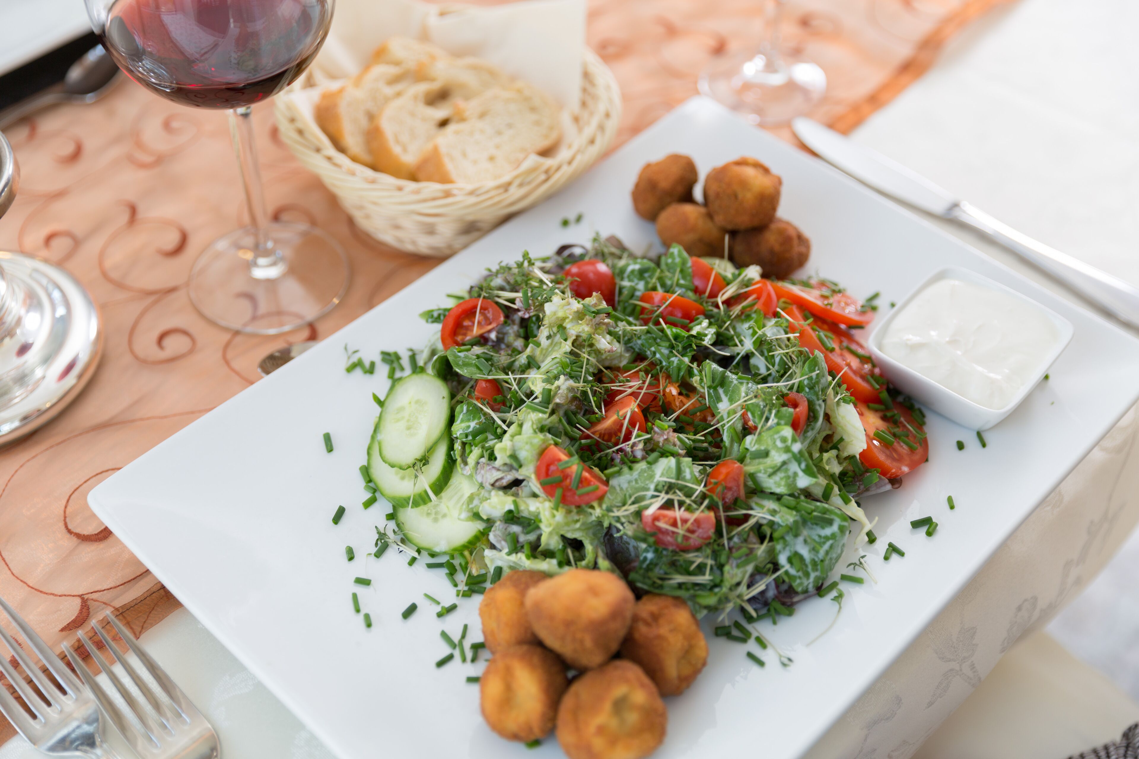 Um prato retangular branco com uma salada, pão e uma pequena tigela de molho.