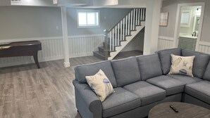 Uma sala de estar moderna com um sofá seccional cinza, mesa de bilhar e escada para um andar superior.