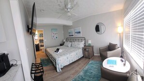 Quarto com cama, mesa de cabeceira, cadeira e uma pequena mesa redonda com abajur.