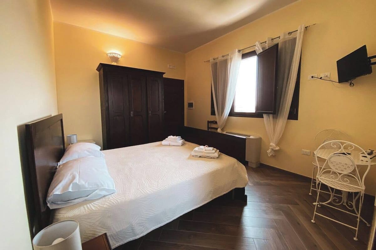 Quarto com cama, cadeira, televisão e janela com cortinas.