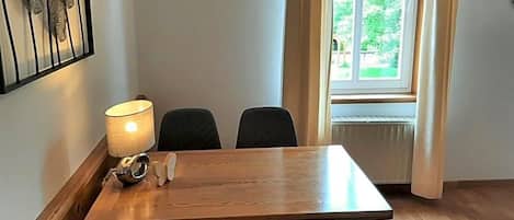 Uma sala de jantar com uma mesa e cadeiras de madeira, uma luminária e uma janela com cortinas.