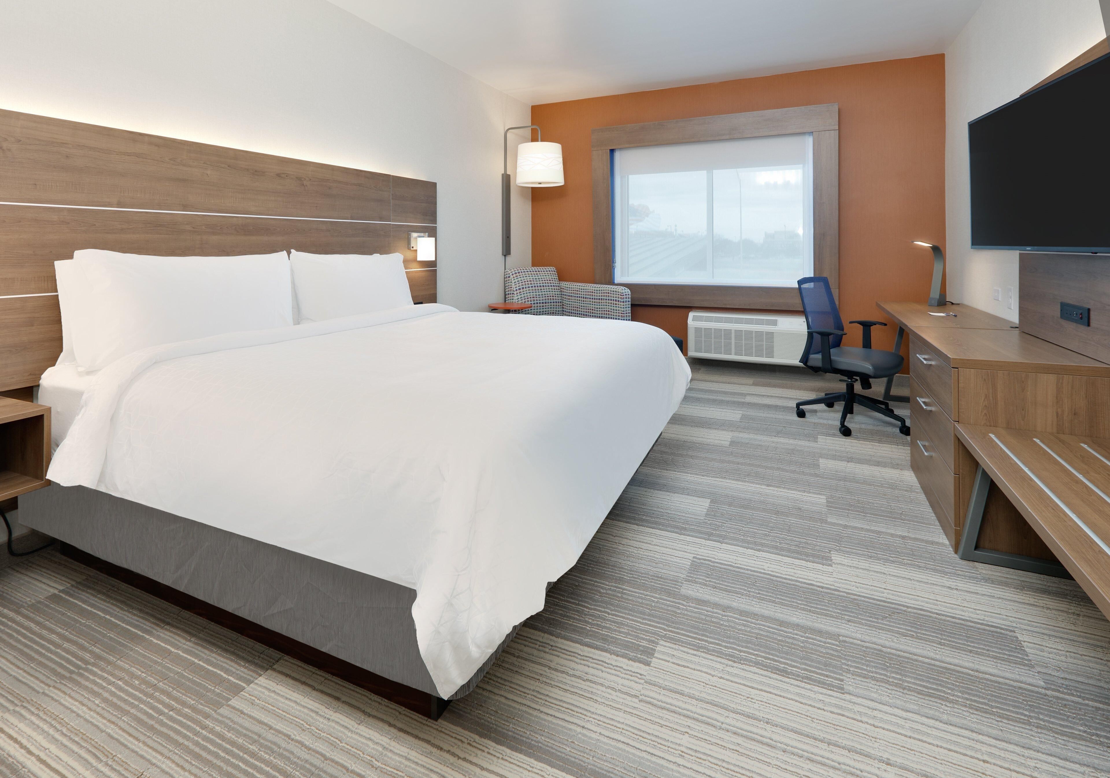 Quarto de hotel com uma cama grande, uma escrivaninha com cadeira, uma televisão e uma janela com vista para o exterior.