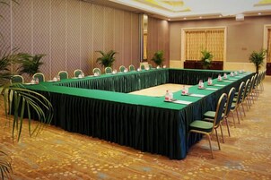 Sala de conferência com uma mesa comprida, cadeiras e plantas.