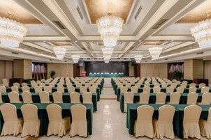 Uma sala de conferências com fileiras de mesas e cadeiras, um palco com um púlpito e lustres.