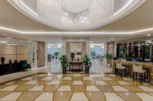 Um saguão de hotel com piso xadrez, área de bar e um grande lustre.