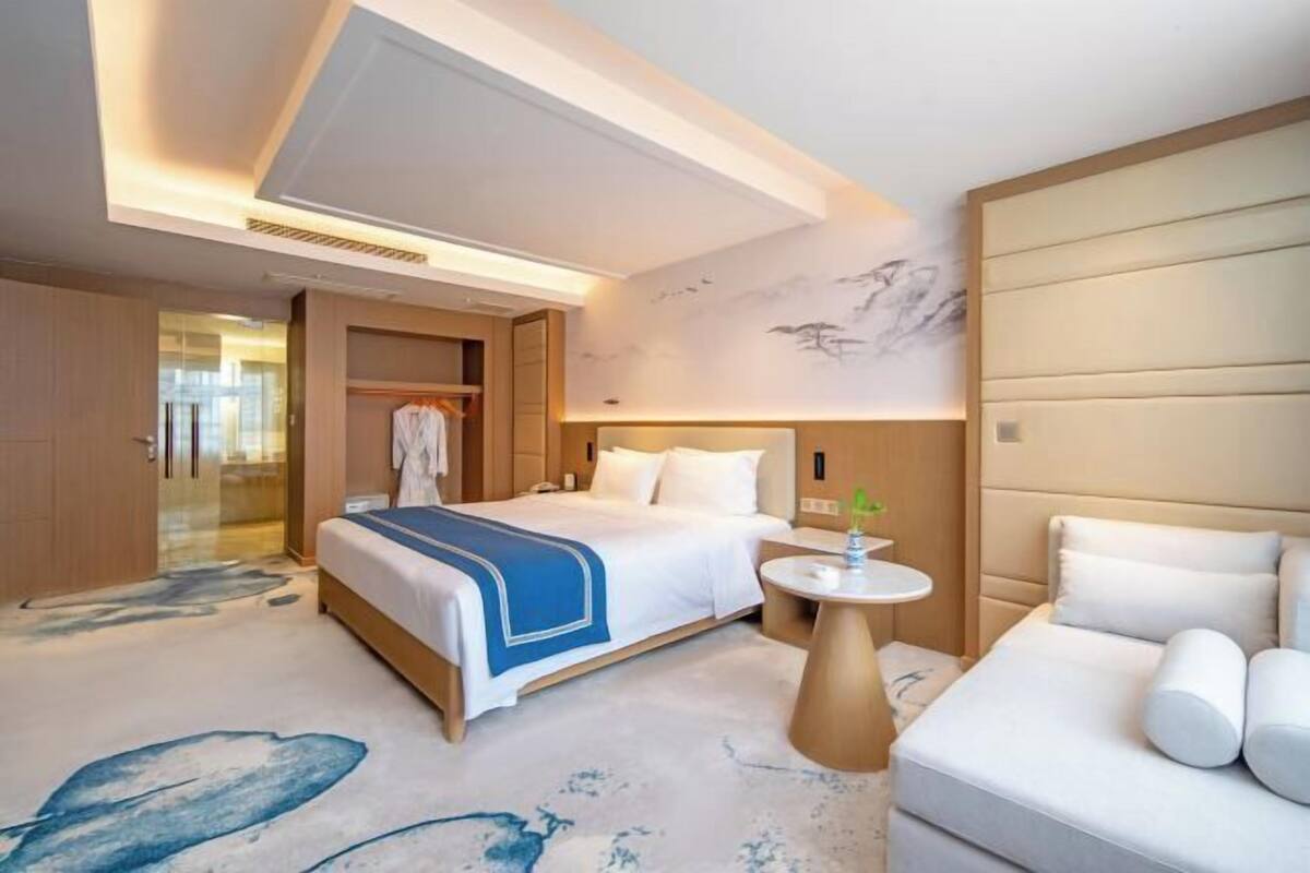 Quarto de hotel moderno com cama, mesa de cabeceira e sofá.