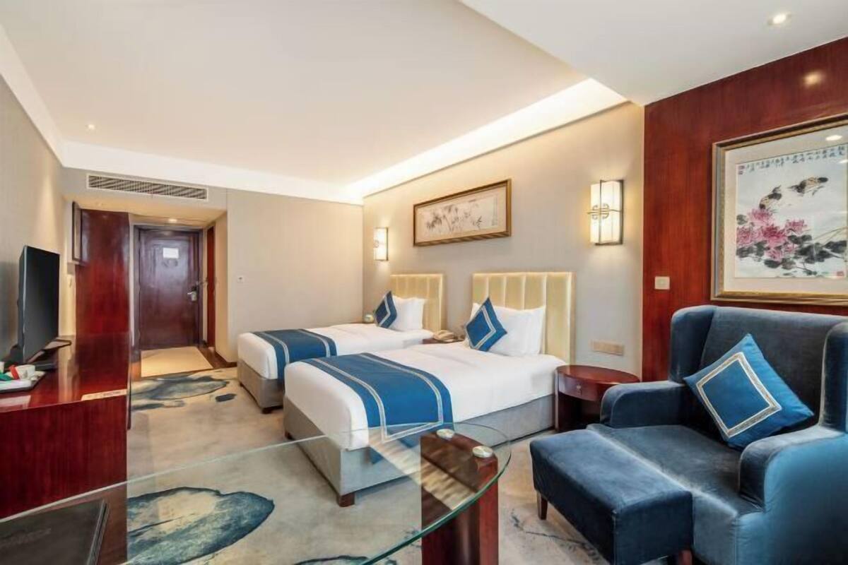 Quarto de hotel com duas camas, uma escrivaninha, uma cadeira e uma televisão.