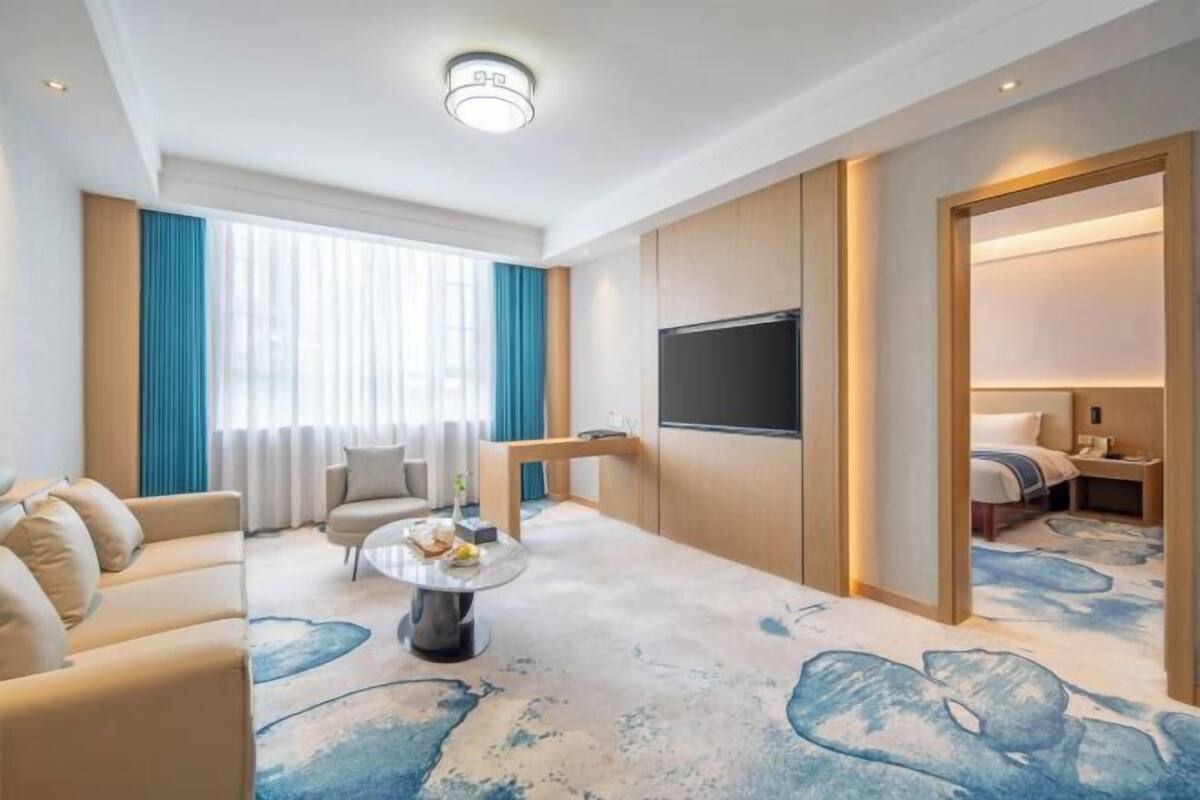 Quarto de hotel moderno com sofá, mesa de centro, televisão e cama.