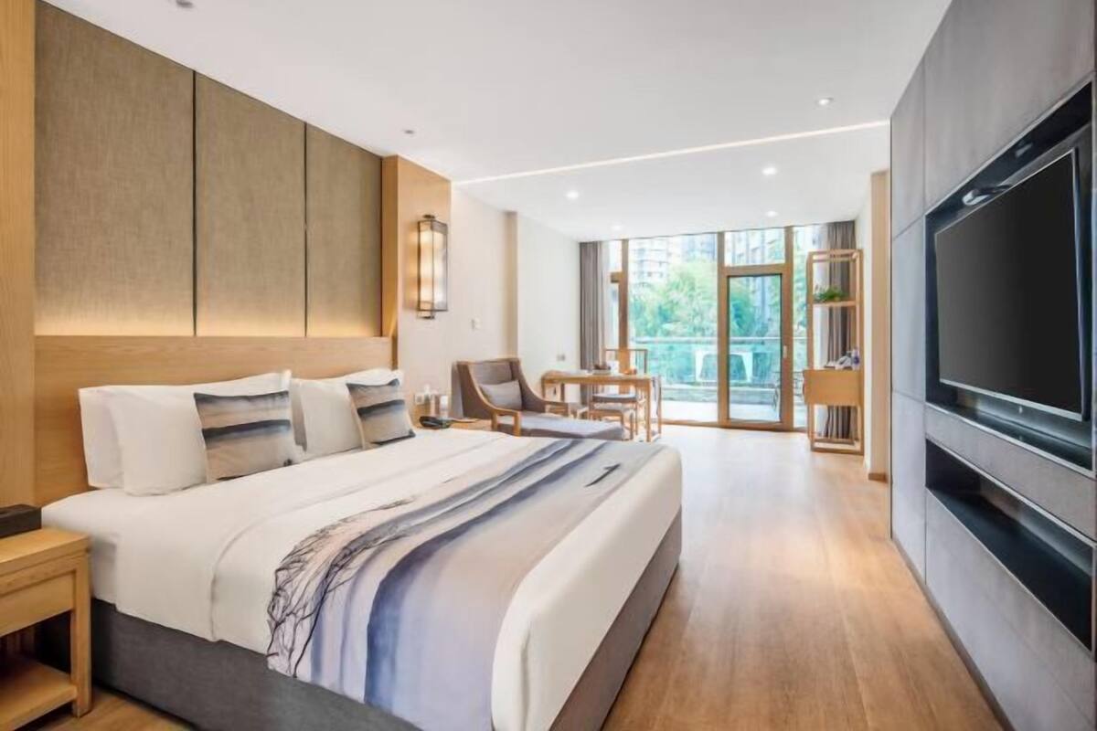 Quarto de hotel moderno com uma cama grande, televisão, escrivaninha e vista para o exterior.