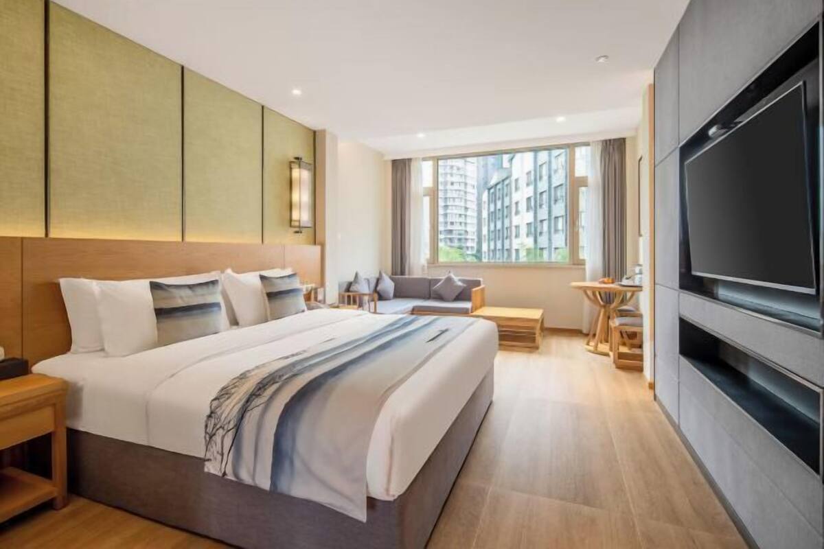 Quarto de hotel com uma cama grande, televisão, escrivaninha e janela com vista para a cidade.