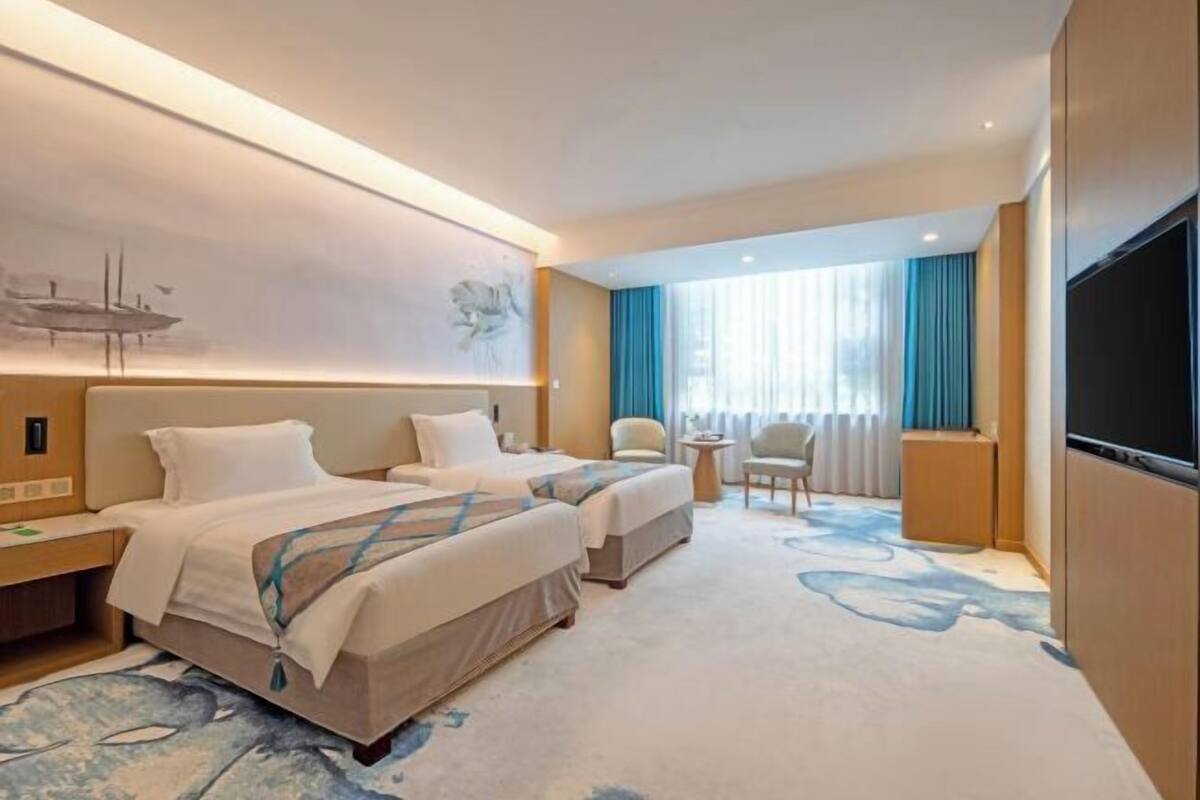 Quarto de hotel com duas camas, uma televisão de tela plana, uma mesa pequena e uma janela com cortinas.