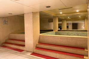 Um banheiro público com piso de azulejos, um banco e uma placa na parede.