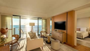 Uma sala de estar ampla com uma televisão grande, assentos confortáveis, uma área de jantar e uma varanda com vista para o mar.