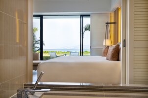 Quarto de hotel moderno com uma cama grande, vista para o exterior e uma varanda com assentos.