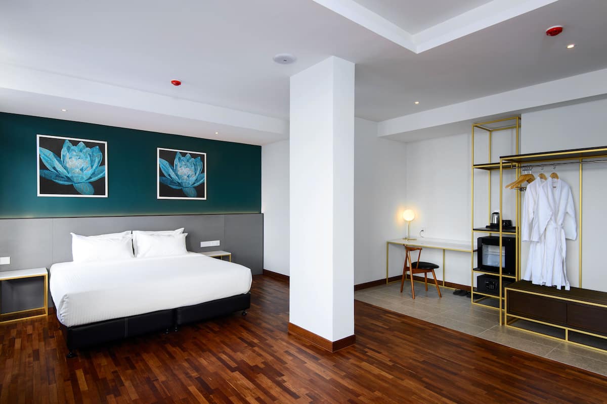 Quarto de hotel moderno com uma cama grande, uma escrivaninha com cadeira, um guarda-roupa com roupões e obras de arte na parede.