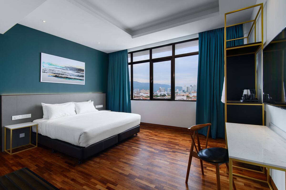 Quarto de hotel moderno com uma cama grande, uma escrivaninha e vista para a cidade.