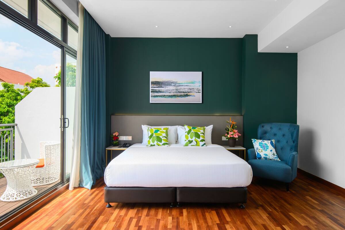 Quarto moderno com uma cama grande, uma mesa de cabeceira, uma cadeira e uma varanda com mobiliário de exterior.