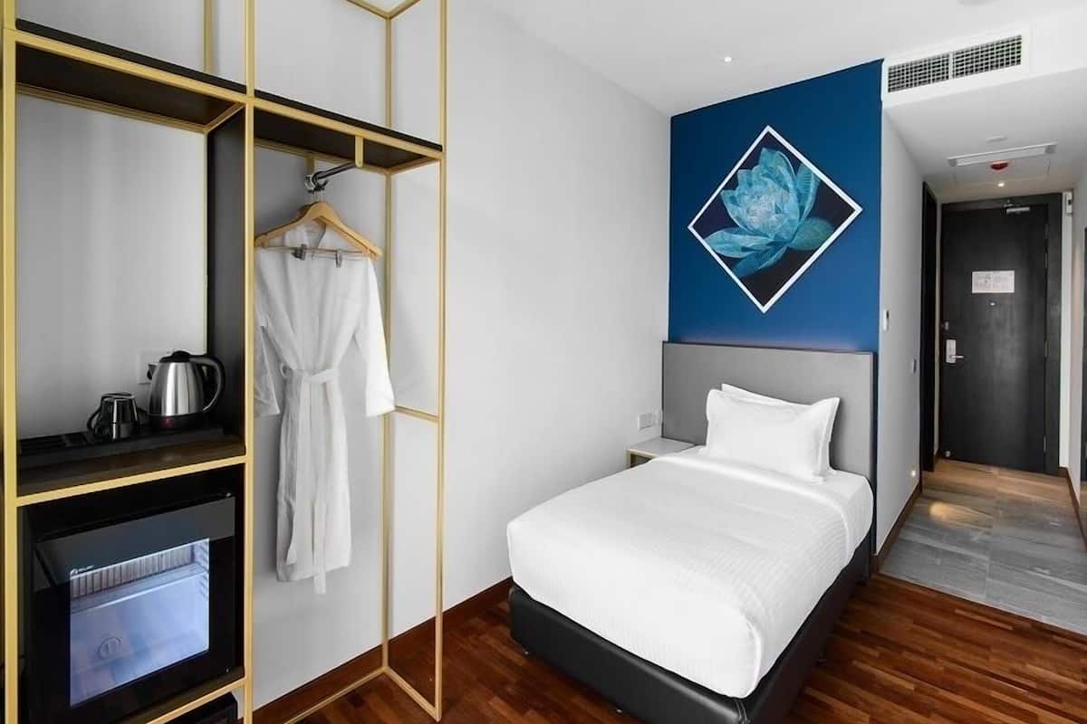 Quarto de hotel moderno com cama, televisão, roupão pendurado em um suporte e obra de arte na parede.