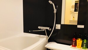 Casa de banho com uma banheira branca, chuveiro manual, lavatório branco com espelho acima e um armário com produtos de higiene pessoal.