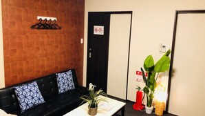 Um hall de hotel com um sofá de couro preto, uma mesa branca com uma planta e um extintor de incêndio.