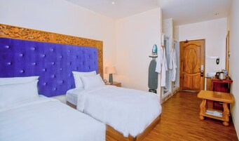 Quarto de hotel com duas camas, uma porta de madeira, uma mesinha e um espelho.