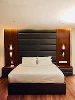 Um quarto moderno com uma cama grande, cabeceira de madeira e abajures laterais.