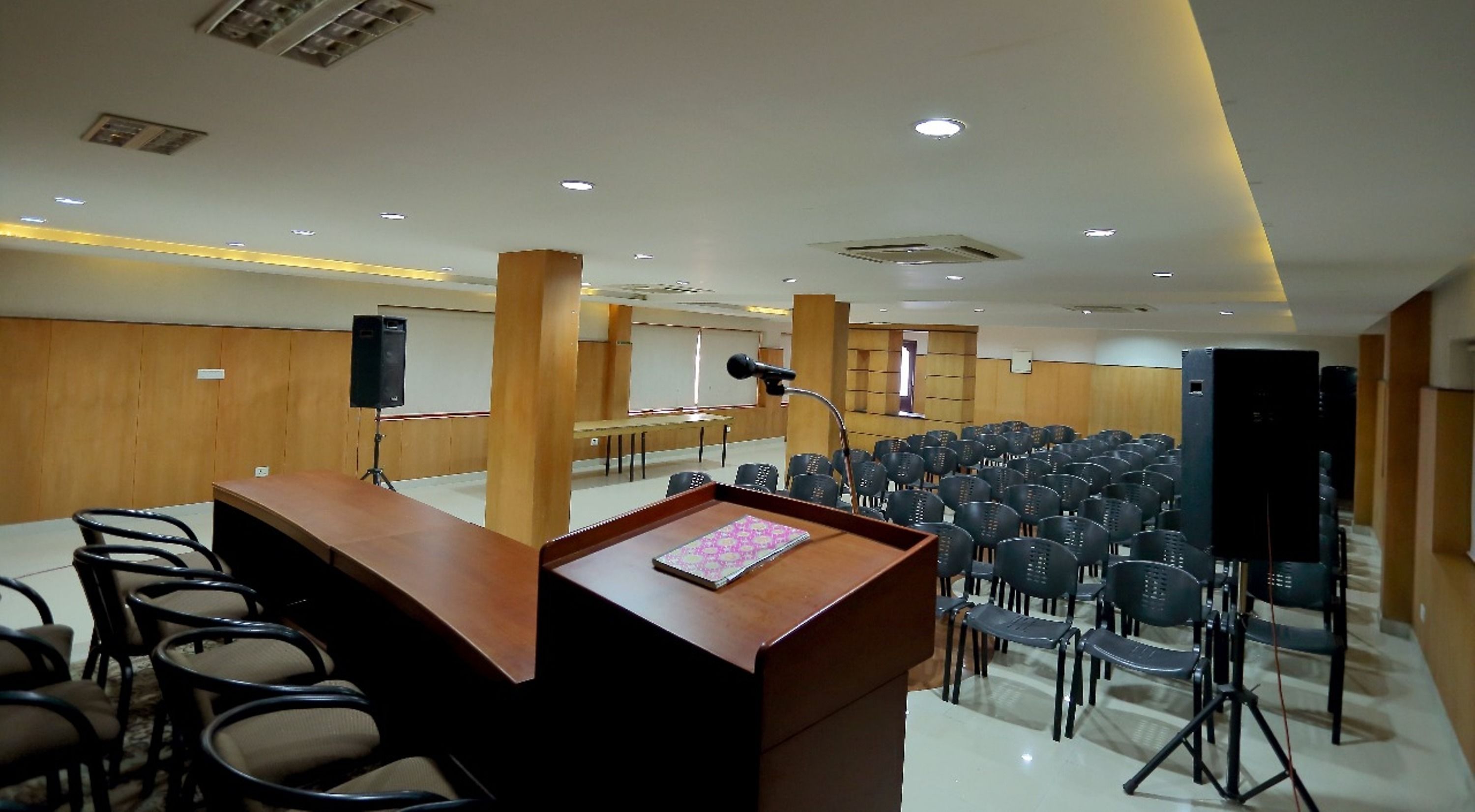 Uma sala de conferências com pódio, fileiras de cadeiras, palco com pódio e quadro branco.