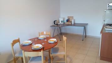 Uma sala de jantar com uma mesa redonda, quatro cadeiras e uma cozinha com cafeteira e armários.