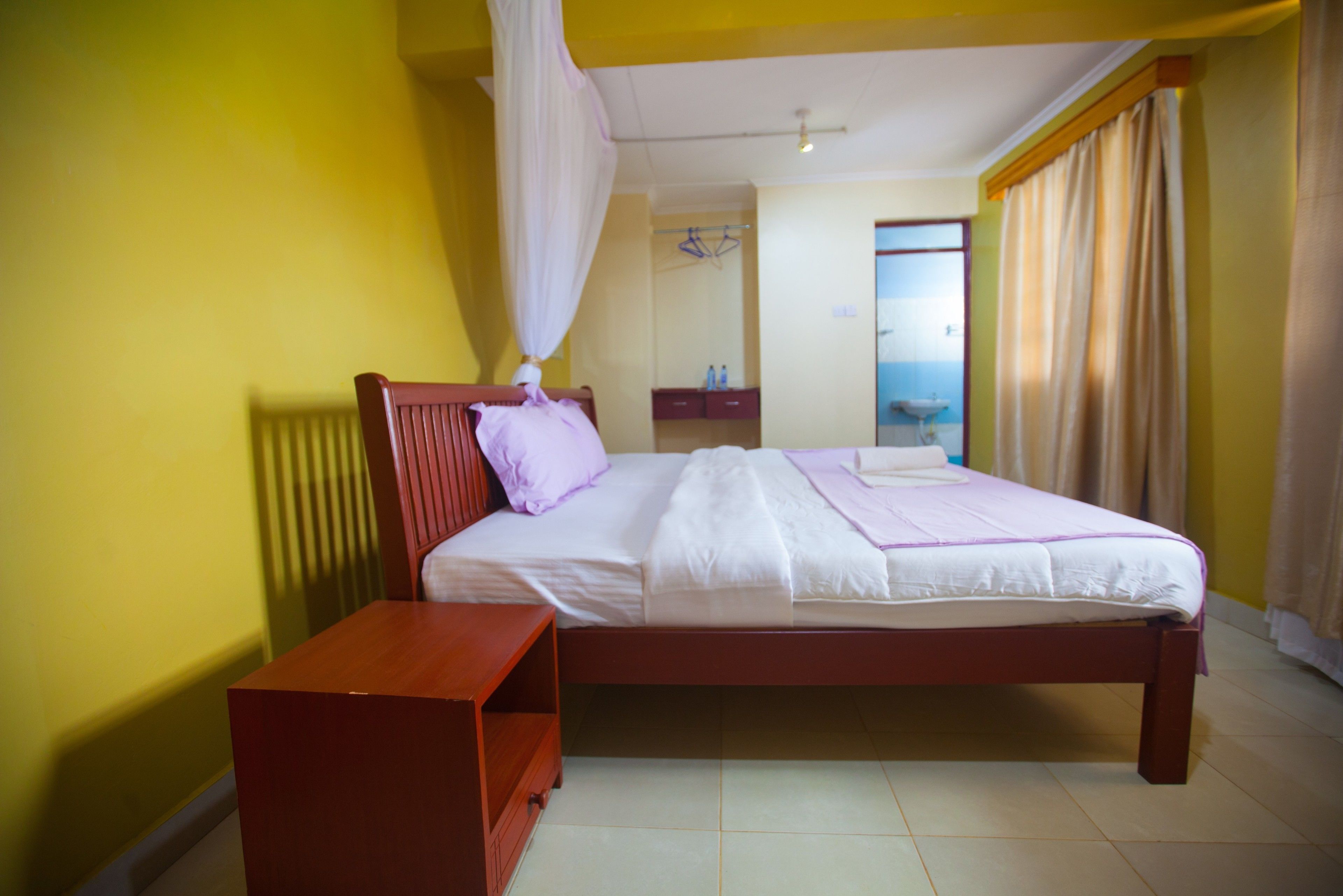Quarto com cama, mesa de cabeceira, janela com cortinas e vista para o mar.