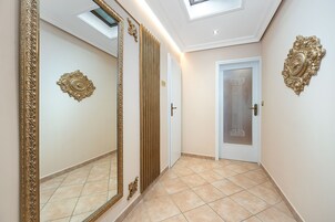 Um corredor com um espelho grande e ornamentado, uma porta com painel de vidro decorativo e um claraboia no teto.