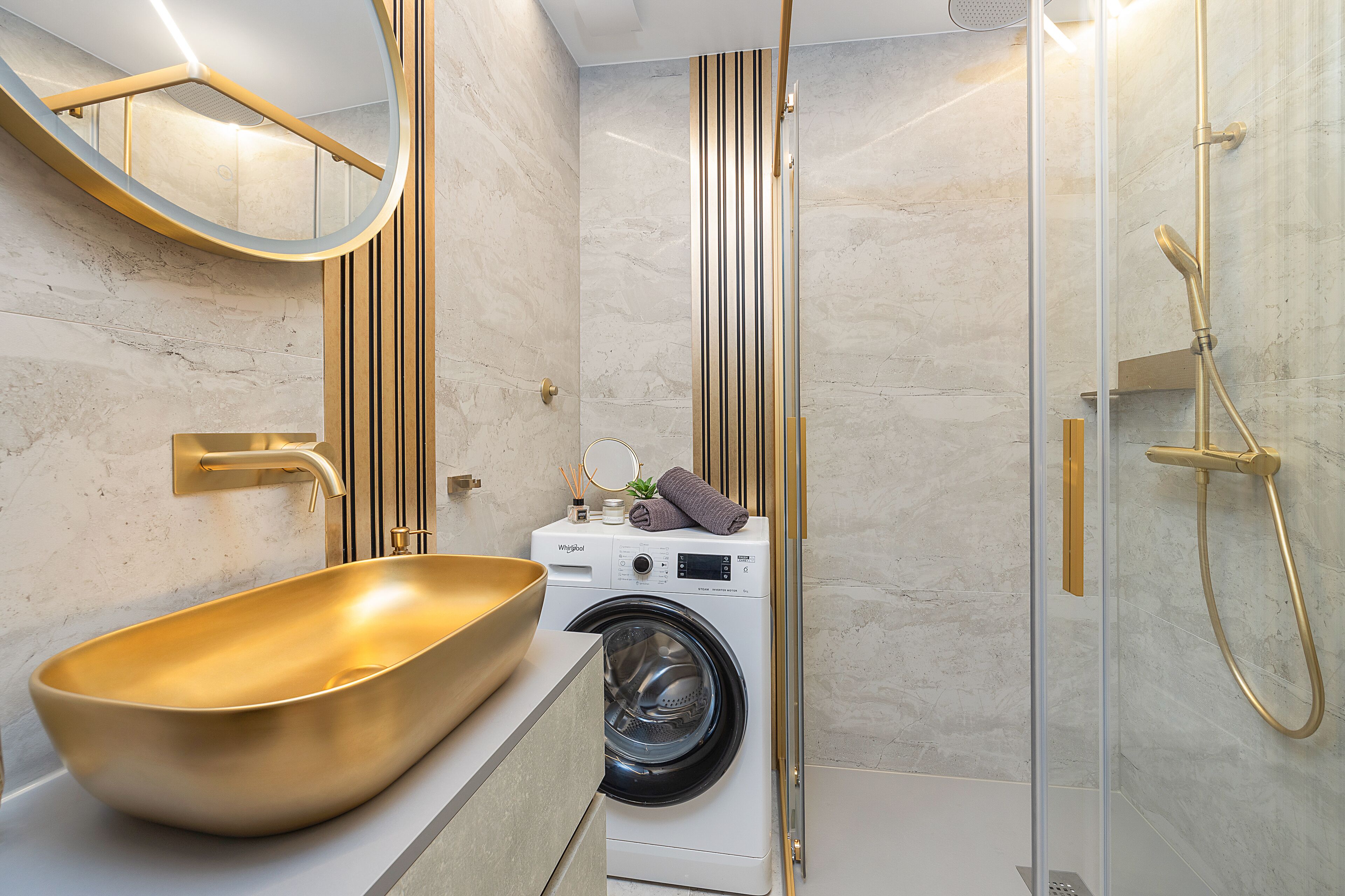 Uma casa de banho moderna com lavatório dourado, máquina de lavar e chuveiro com detalhes dourados.