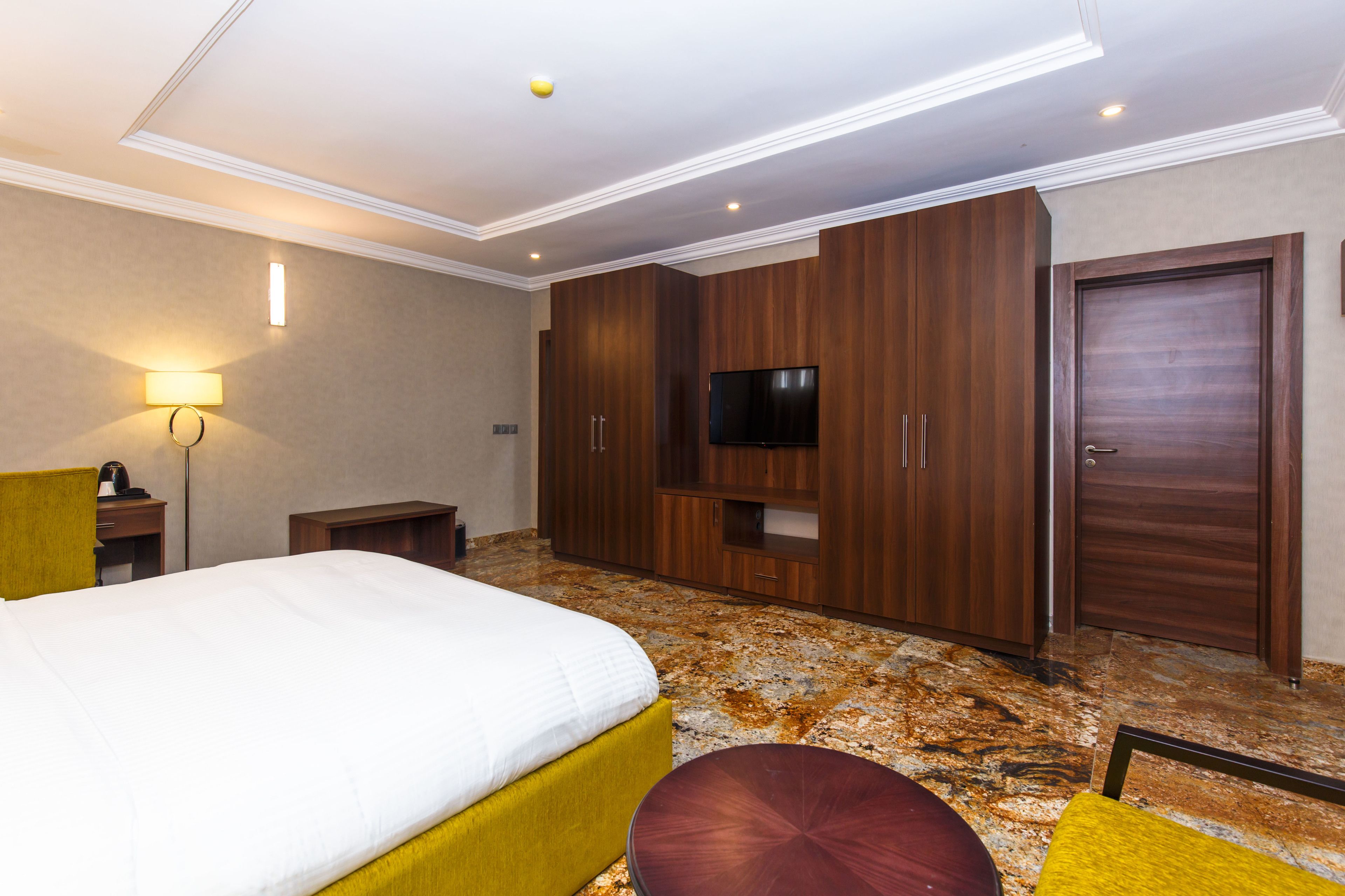 Quarto de hotel com cama grande, guarda-roupa de madeira, televisão de ecrã plano, secretária e candeeiro.