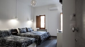 Quarto moderno com duas camas, luminária pendente e janela com vista.