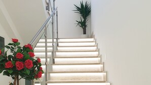Uma escadaria com degraus brancos e corrimão, levando a um patamar com uma planta em vaso.