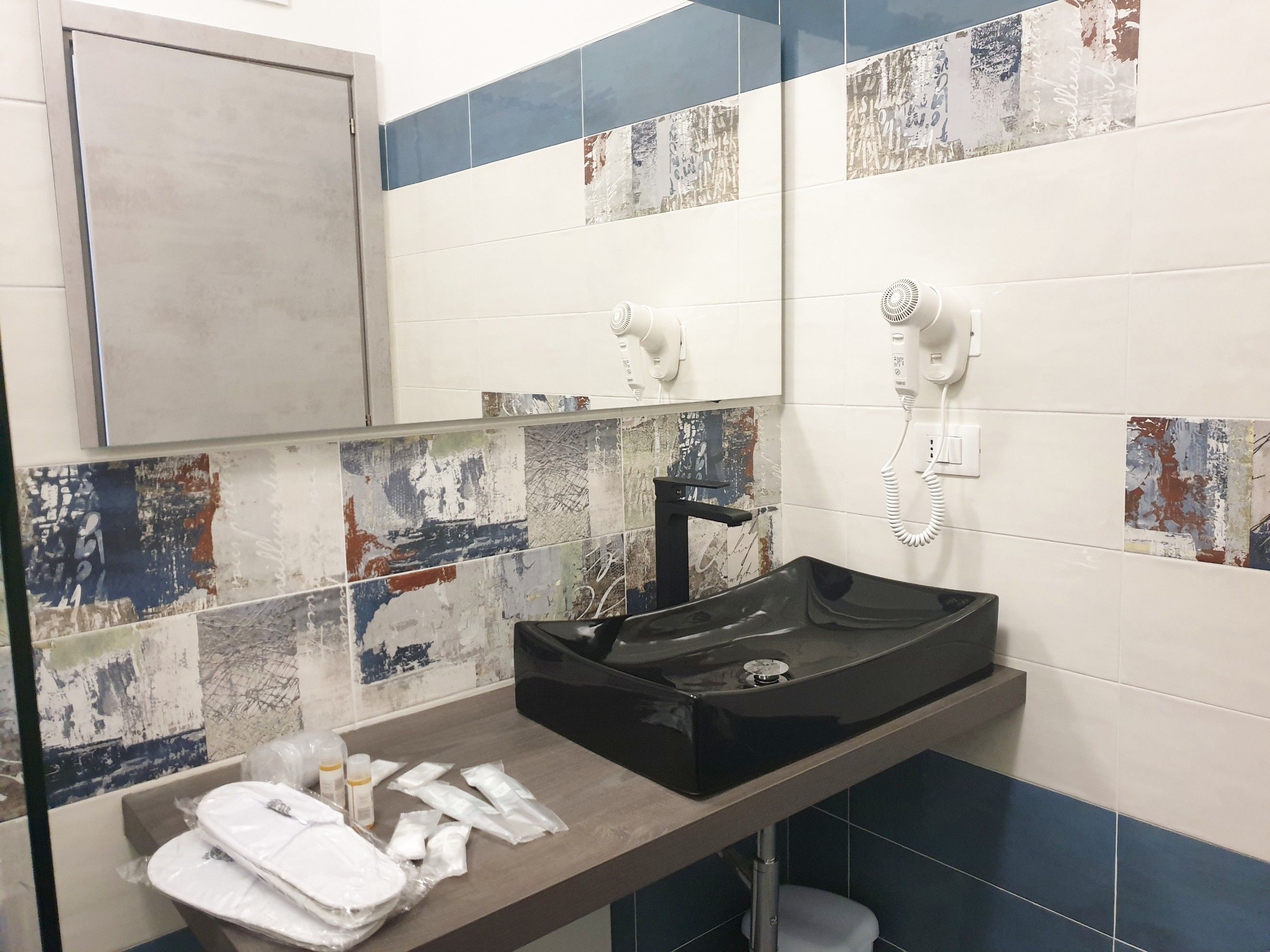 Casa de banho com lavatório, espelho e dois secadores de cabelo fixados na parede.
