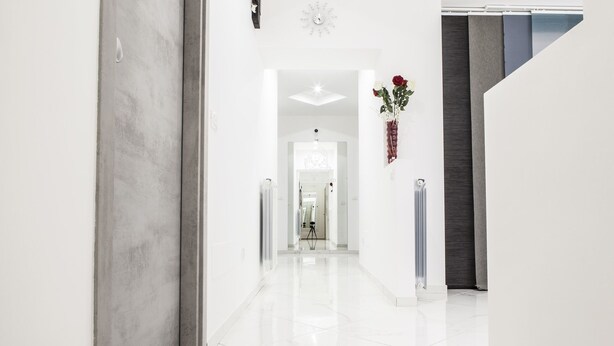 Um corredor moderno e bem iluminado com piso de mármore, que leva a um quarto com uma grande janela e vista para o exterior.