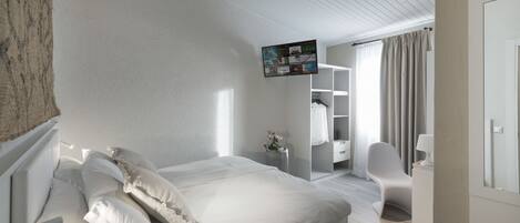Quarto de hotel moderno com uma cama grande, televisão na parede, escrivaninha e uma cadeira.