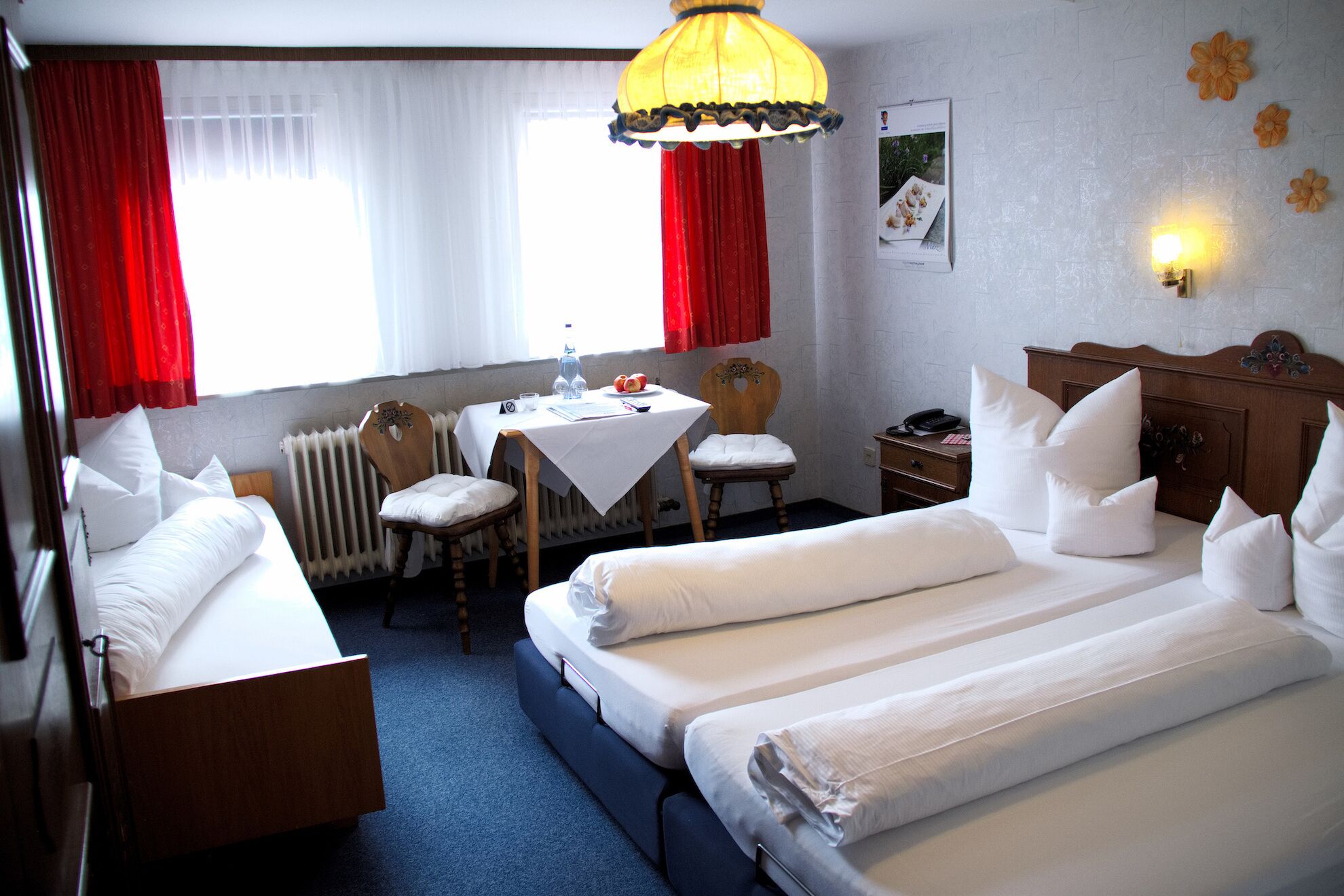 Quarto de hotel com duas camas, uma mesa, uma cadeira, uma escrivaninha e um radiador.