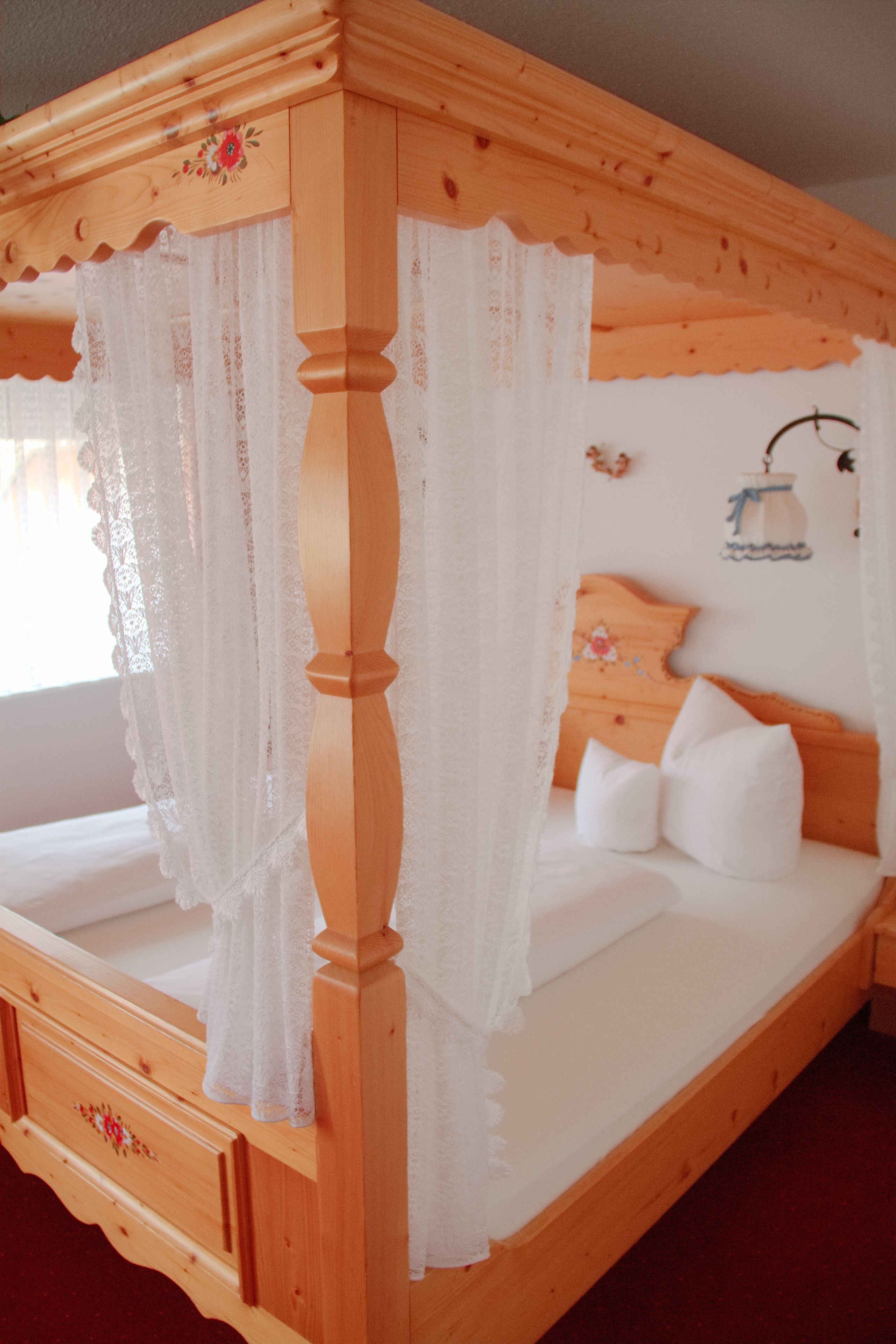 Uma cama de madeira com dossel, roupa de cama branca e cortinas de renda.