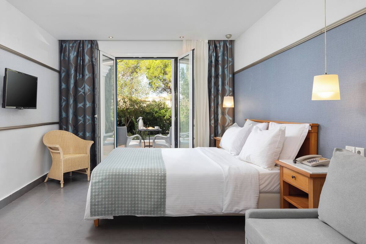 Quarto de hotel com cama, uma cadeira, uma mesa e televisão.