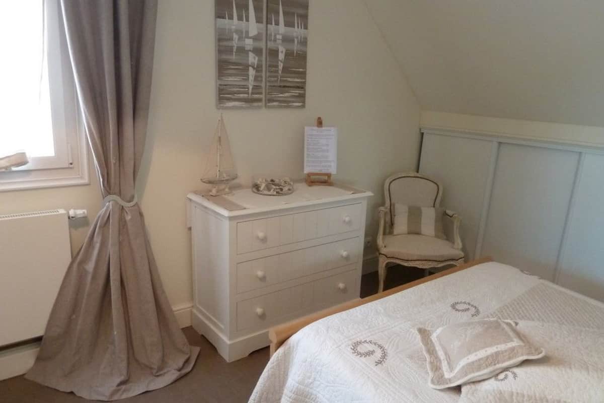 Quarto com uma cama, cômoda, cadeira e janela com cortinas.