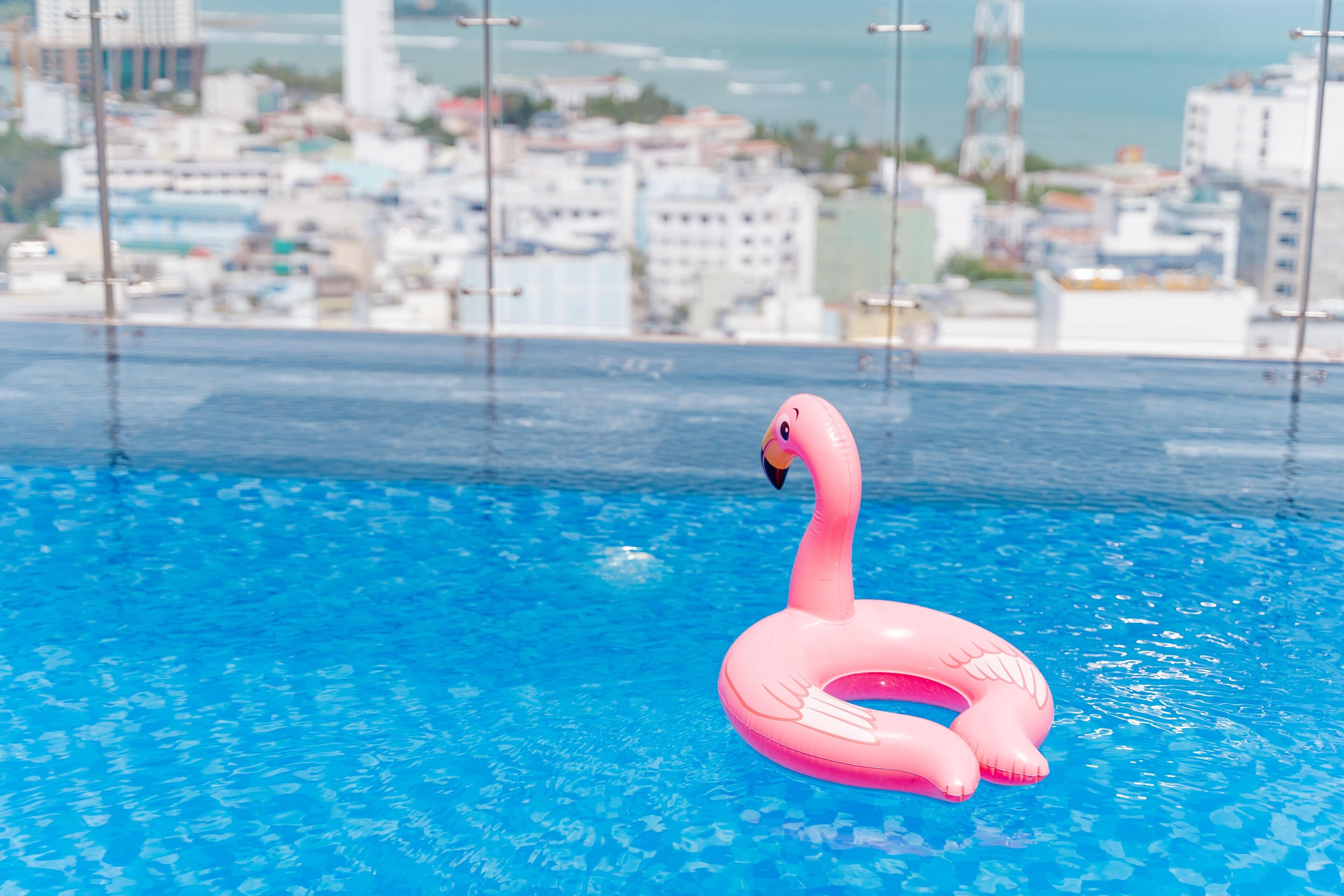Um flutuador de flamingo rosa em uma piscina azul cristalina, com uma vista para o horizonte urbano ao fundo.