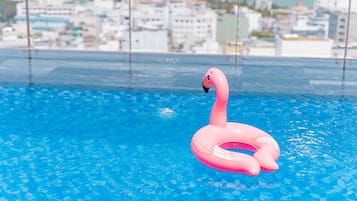 Um flutuador de flamingo rosa em uma piscina azul cristalina, com uma vista para o horizonte urbano ao fundo.