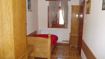 Quarto com estrutura de madeira, uma cama, guarda-roupa de madeira, radiador e janela com cortinas.