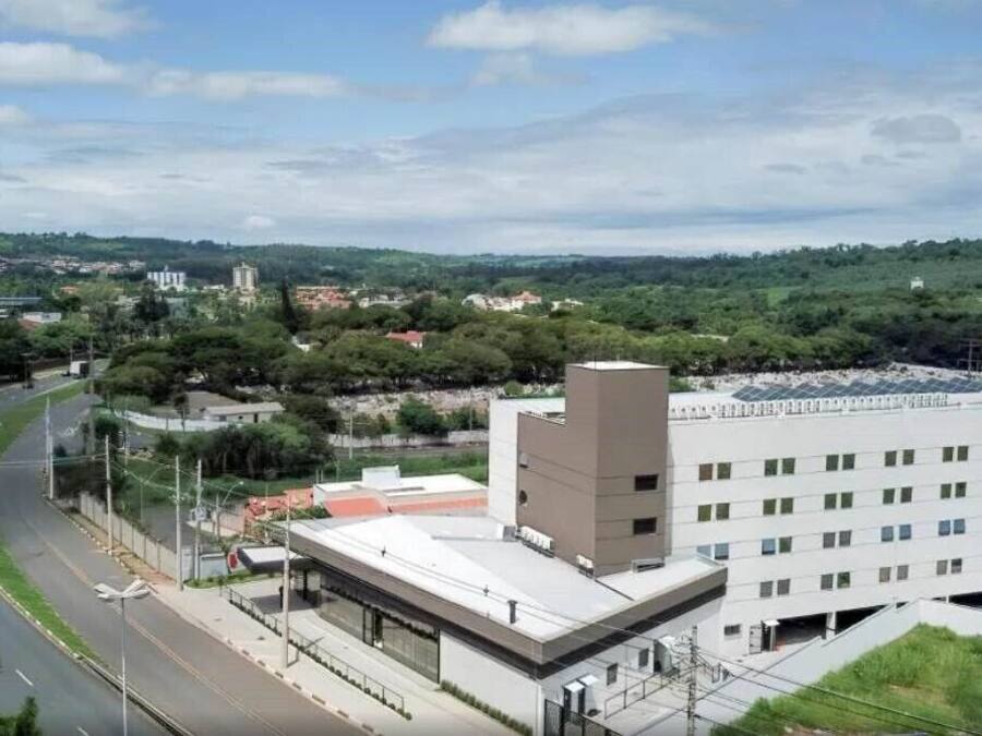 Um edifício moderno com telhado plano e formato retangular, rodeado por uma estrada e vegetação.